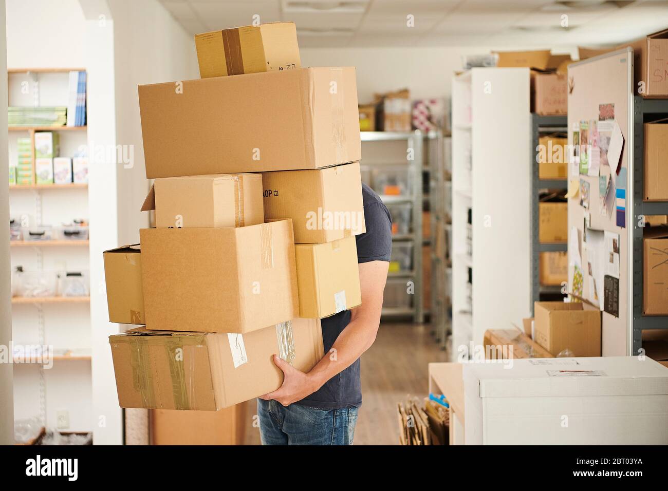 A man carrying a stack of boxes across a store room Stock Photo - Alamy