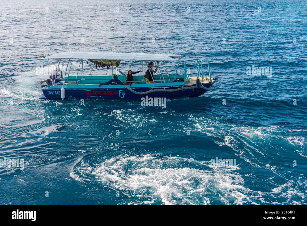 Some tourists on a typical fiji water taxi, boat in deep blue water of ...