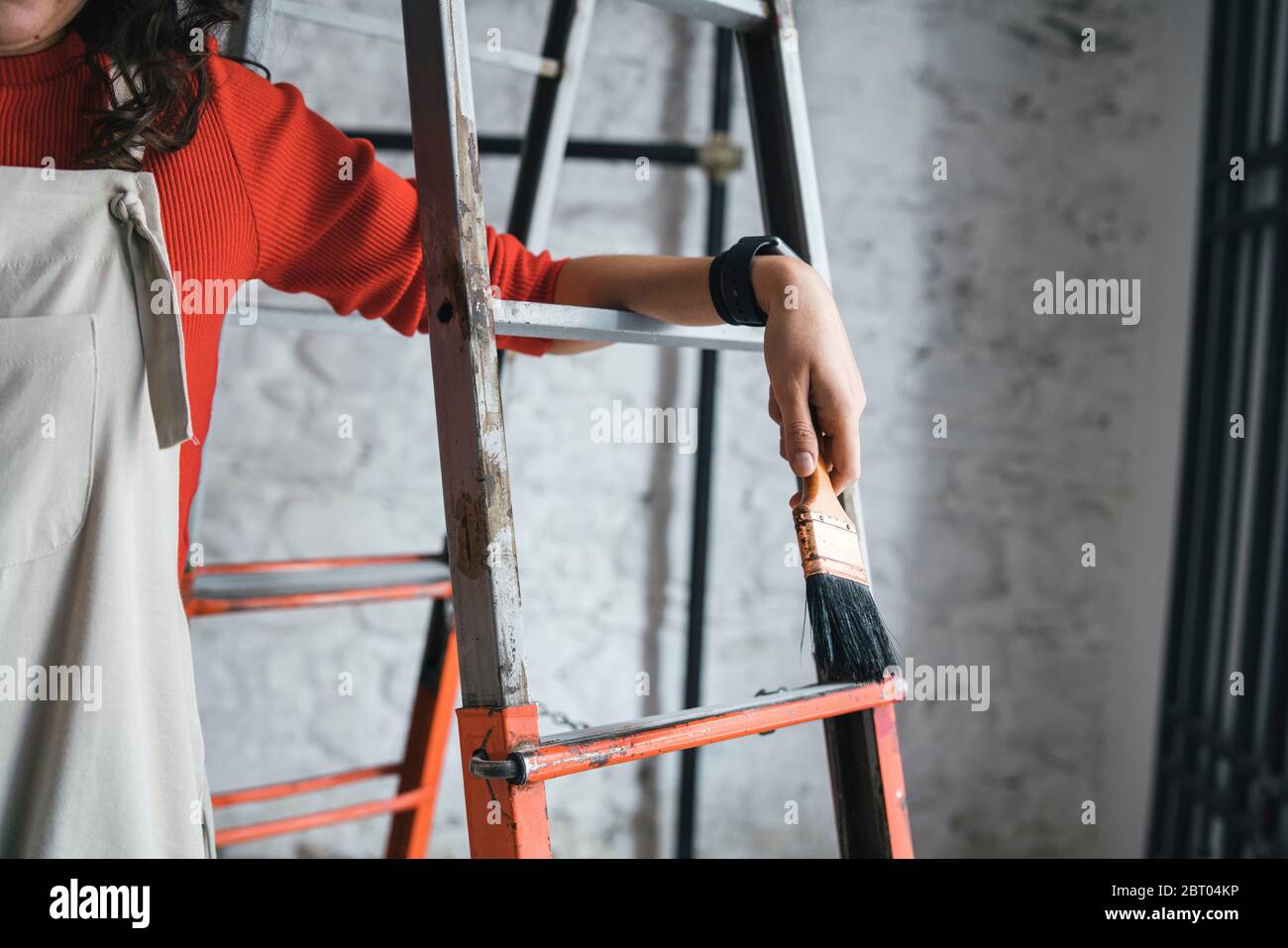 Mid adult woman leaning on step ladder with paint brush in her new shop ...