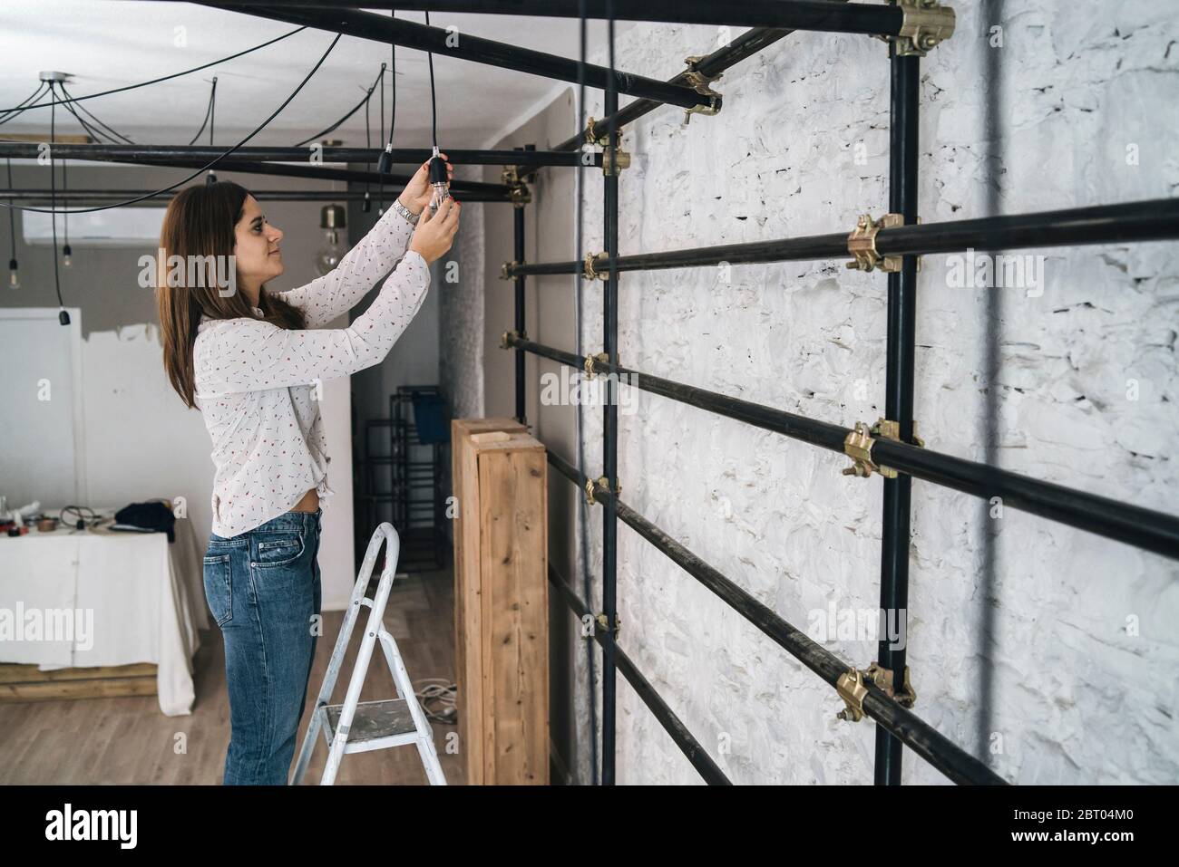 Mid adult woman on step ladder hanging lightbulb in her new shop Stock ...