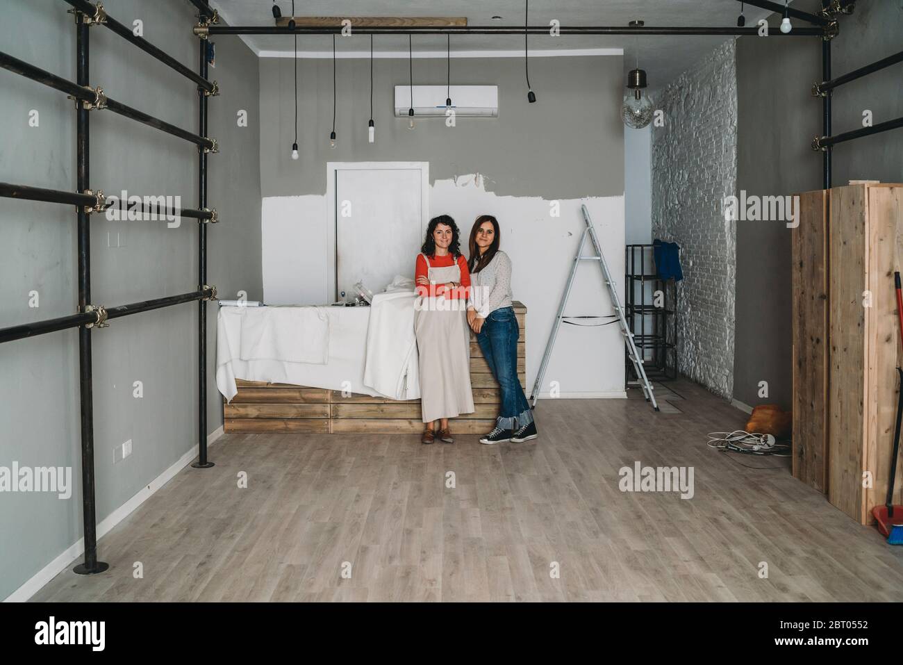 Two mid adult women leaning against table in their new shop, full ...