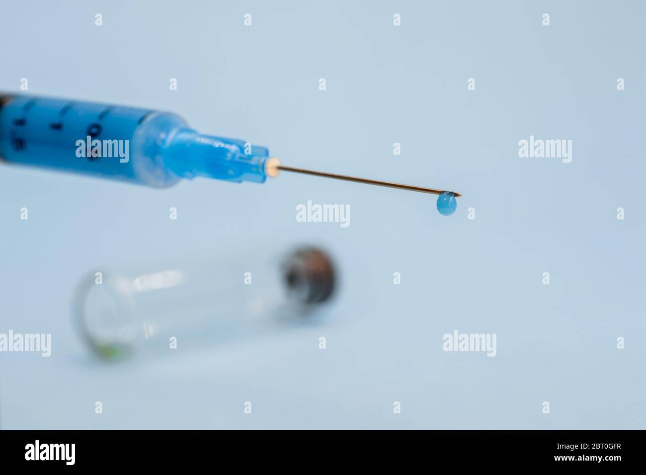 A close-up syringe needle with a drop of solution at the end against an ...