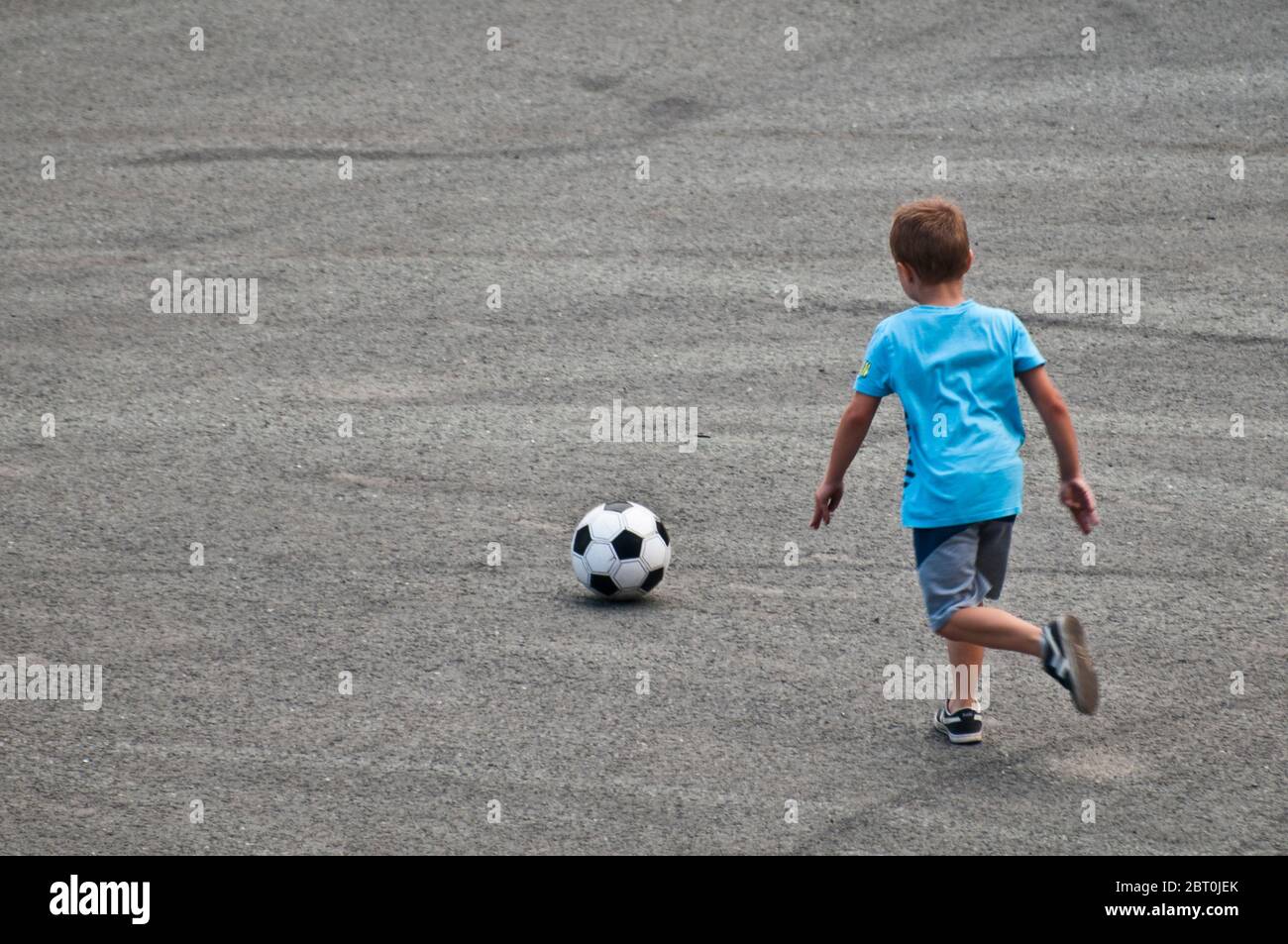 kid in blue shirt and shorts kicking a football ball in the street ...