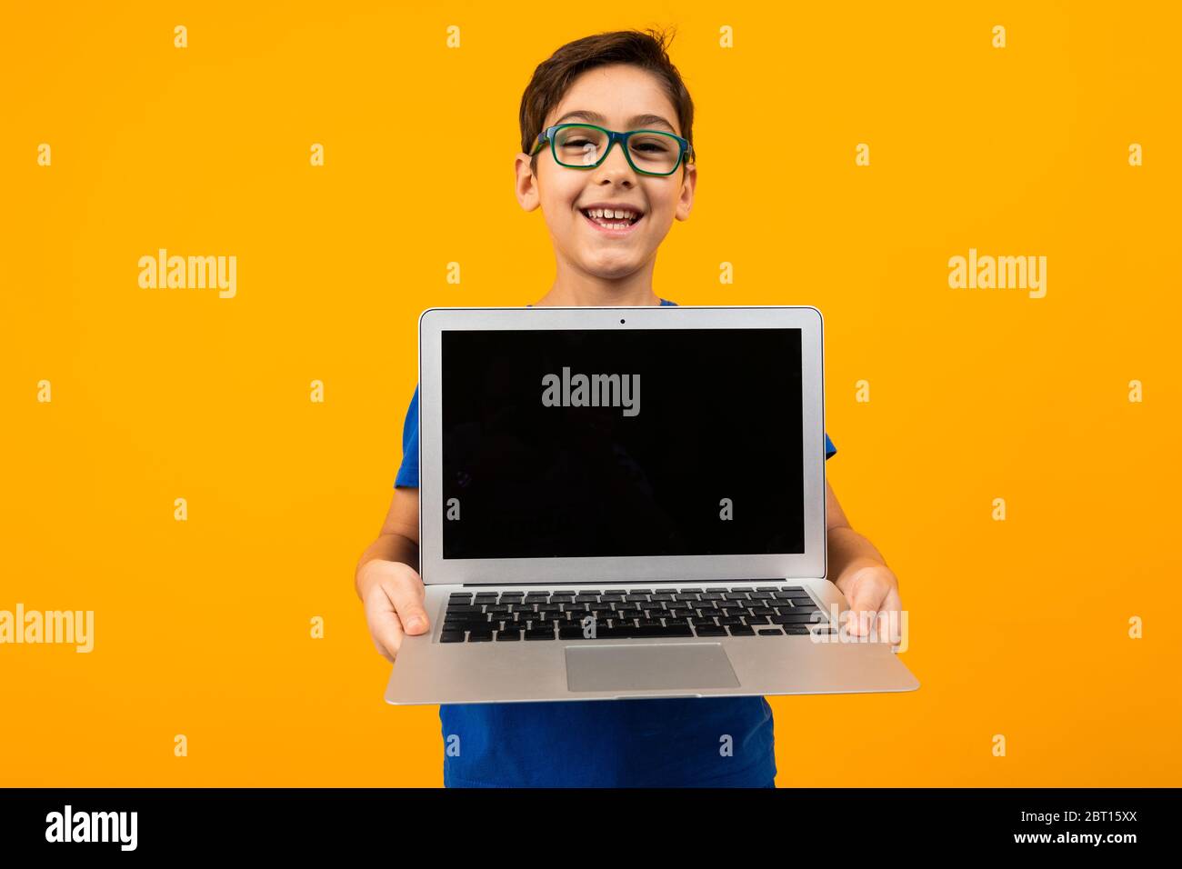 joyful caucasian boy shows laptop screen with mockup on yellow studio ...