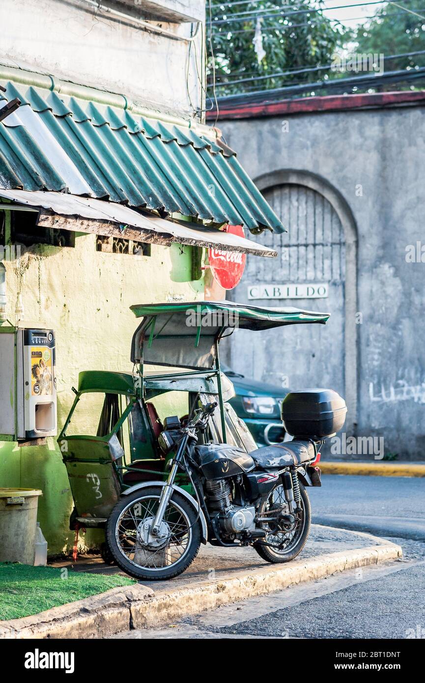A traditional pedicab or rickshaw is parked next to a modern motorbike ...