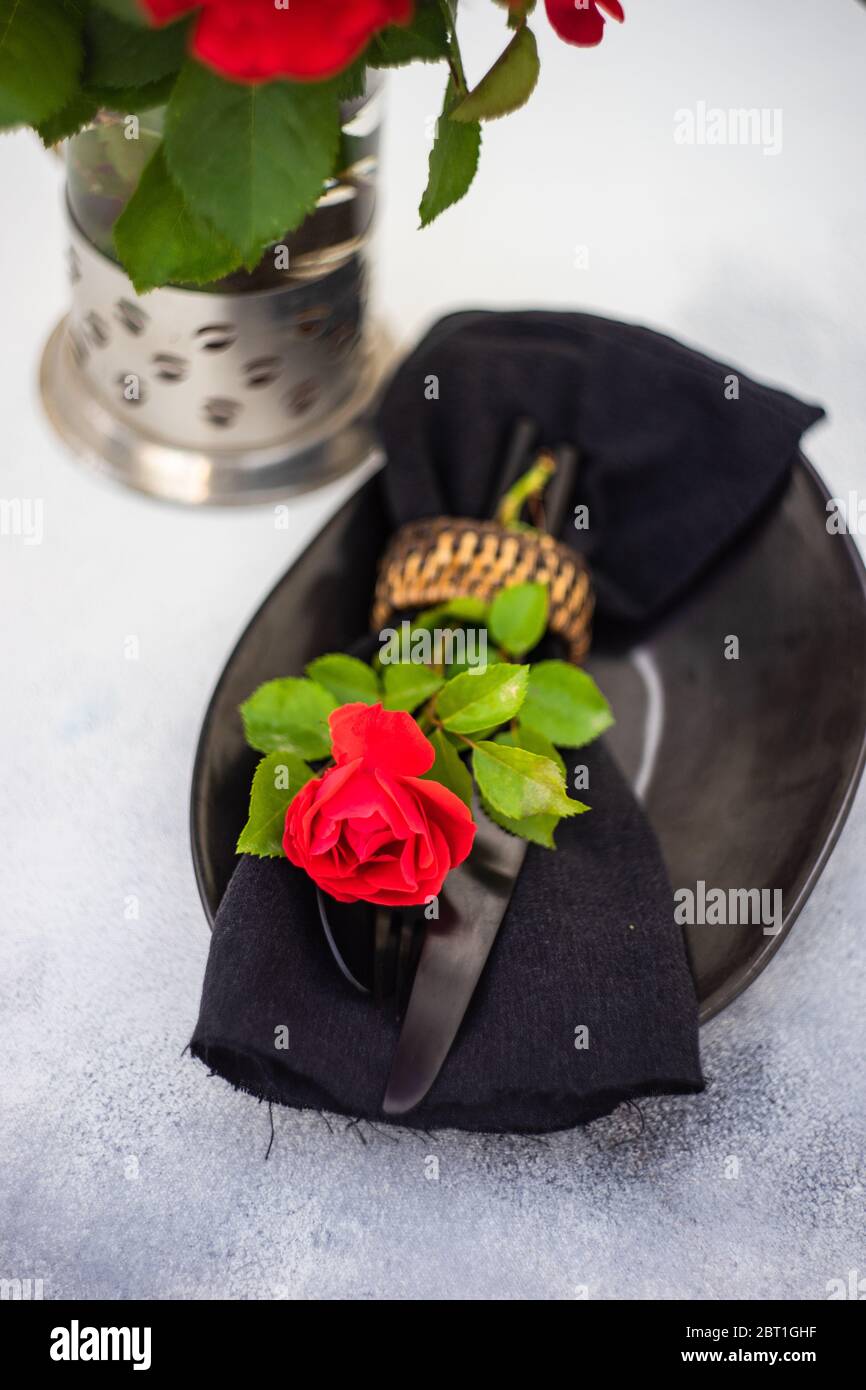 Table setting with fresh red rose flower and black plate and cutlery on ...