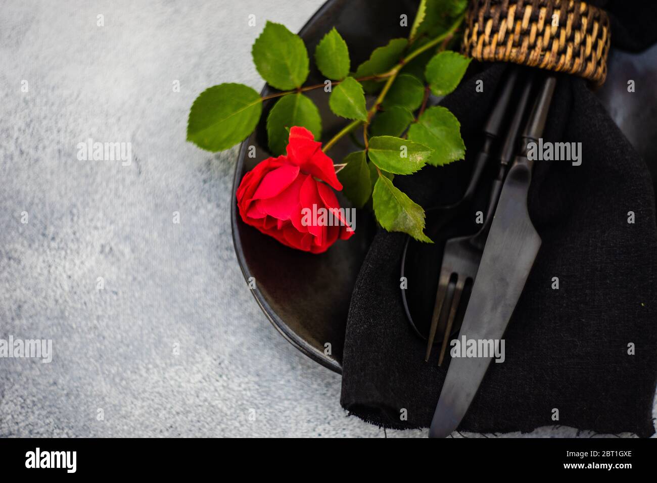 Table setting with fresh red rose flower and black plate and cutlery on ...