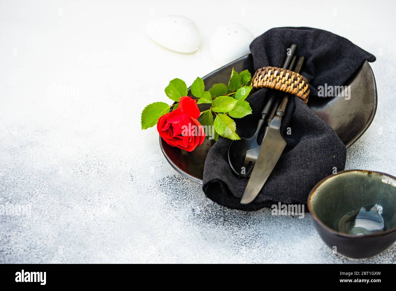 Table setting with fresh red rose flower and black plate and cutlery on ...