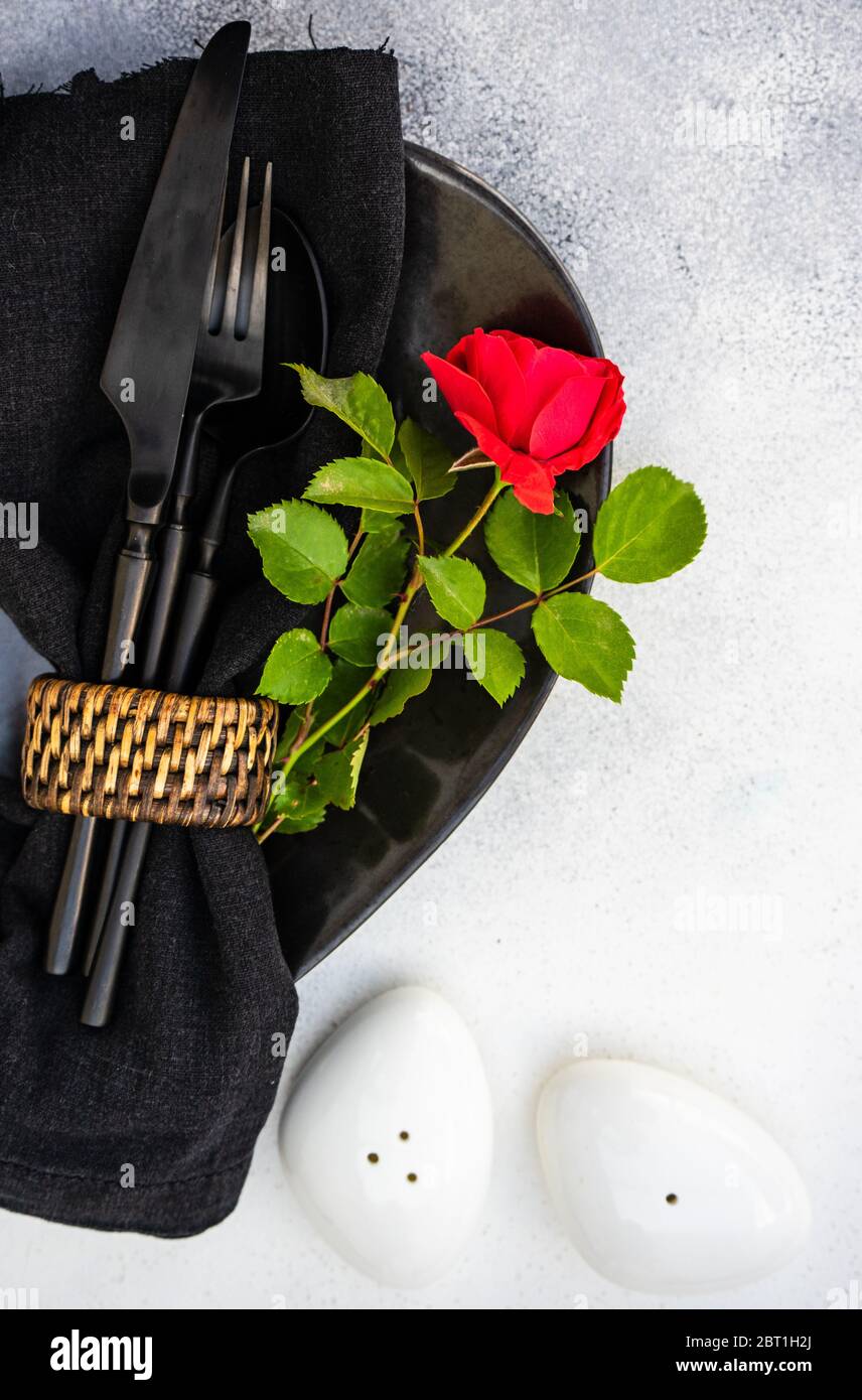 Table setting with fresh red rose flower and black plate and cutlery on ...
