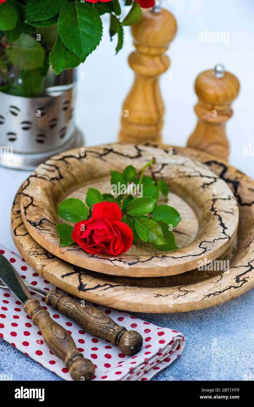 Table setting with fresh red rose flower on vintage wooden plates on ...