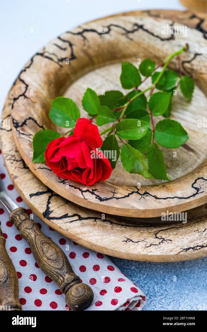Table setting with fresh red rose flower on vintage wooden plates on ...