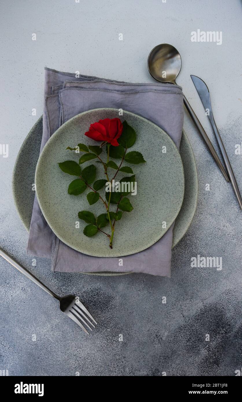 Table setting with fresh red rose flower on stone grey plates on ...