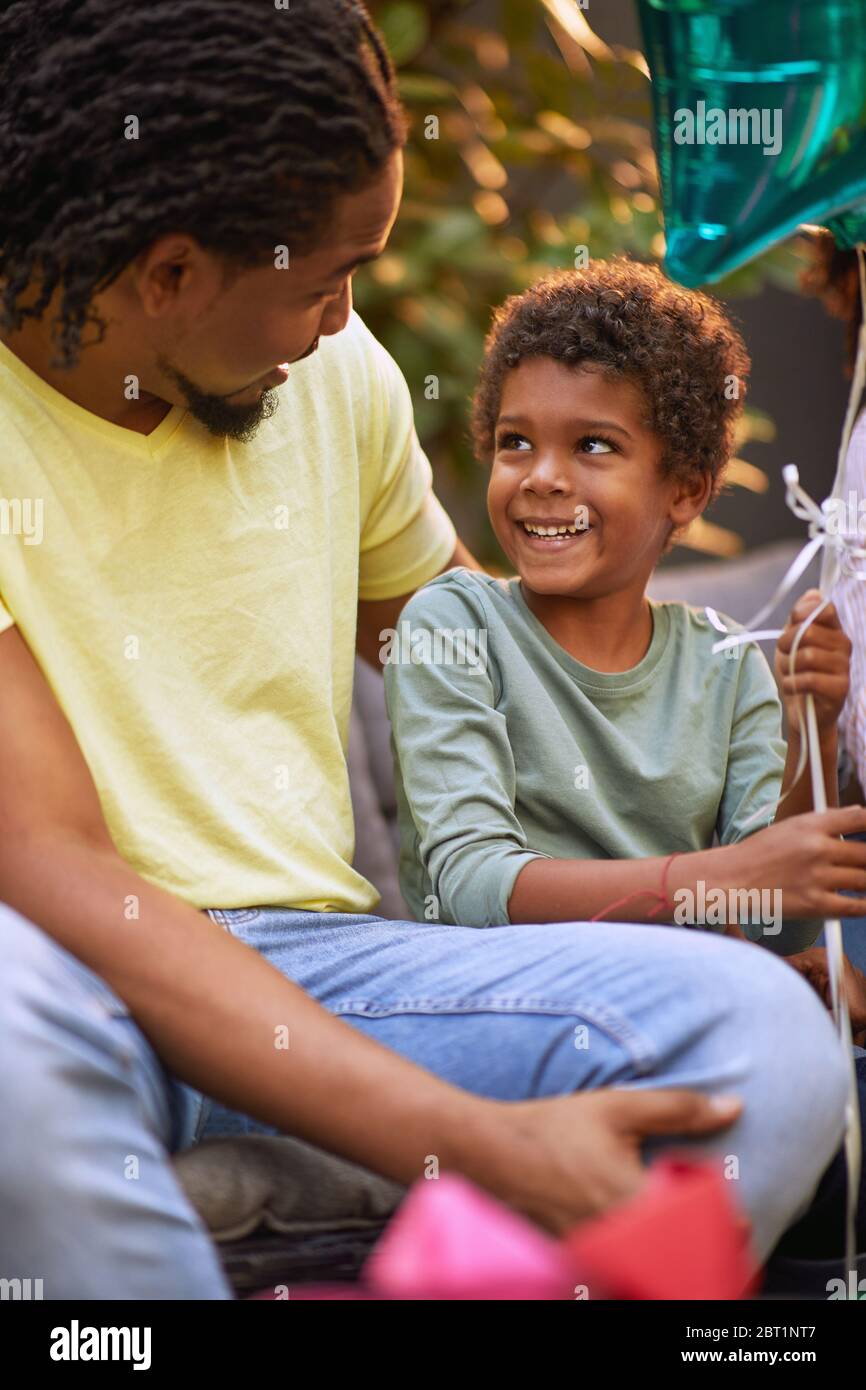 Afro American Father And Son Cuddling And Smiling At Home Enjoying And