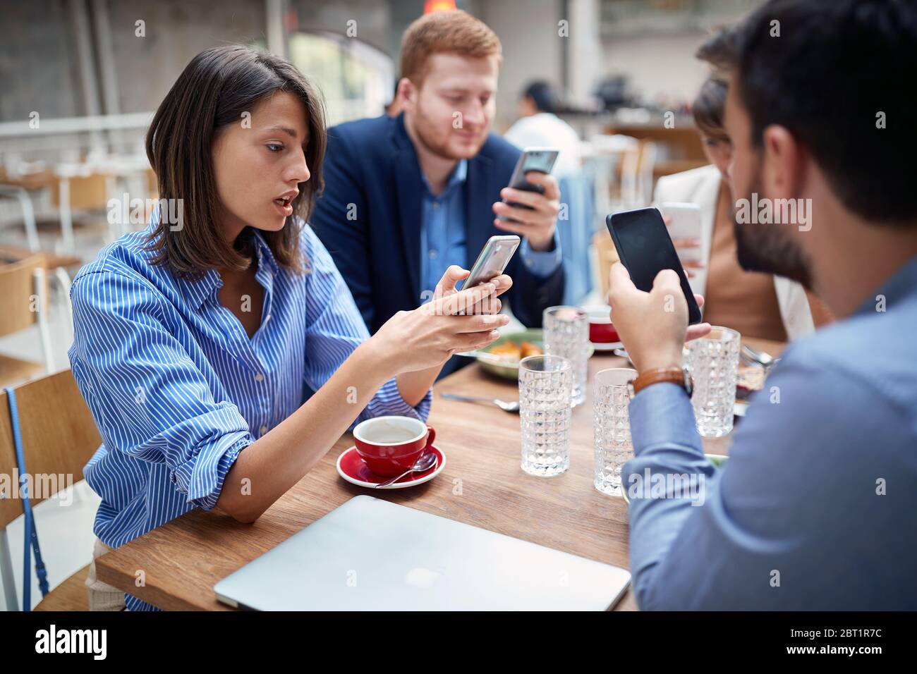 young adult businesspeople at lunch in a restaurant checking their cell ...