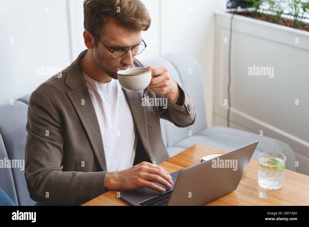Stylish young man drinking coffee and using laptop on cafe Stock Photo ...