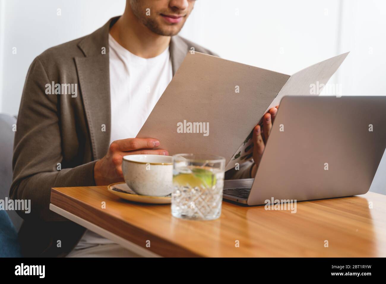 Young man sitting at the table with laptop and reading menu Stock Photo ...