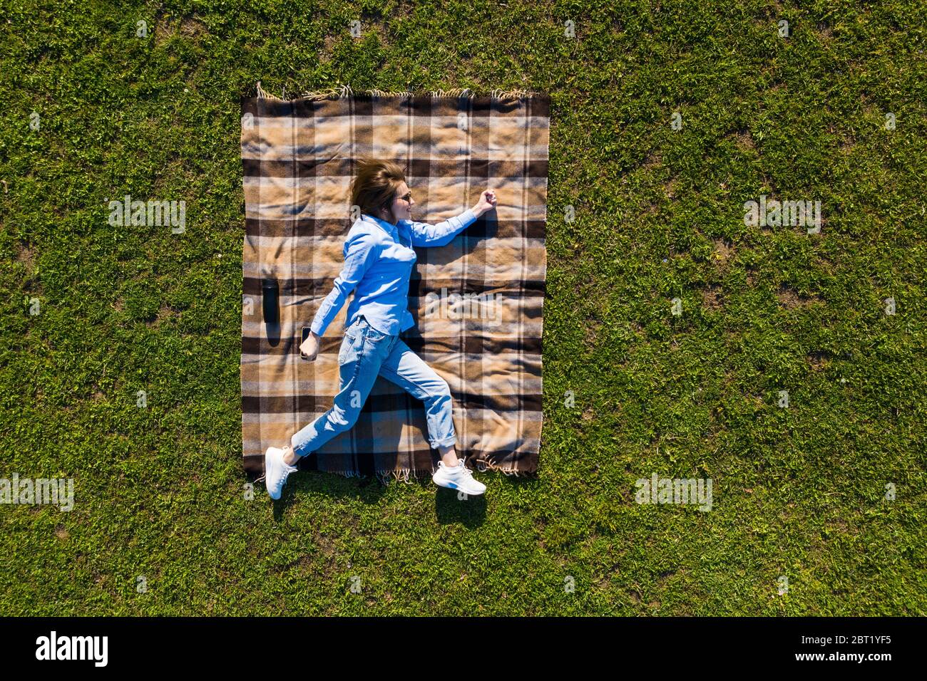 Top view young woman runing and lying on the blanket on green grass ...