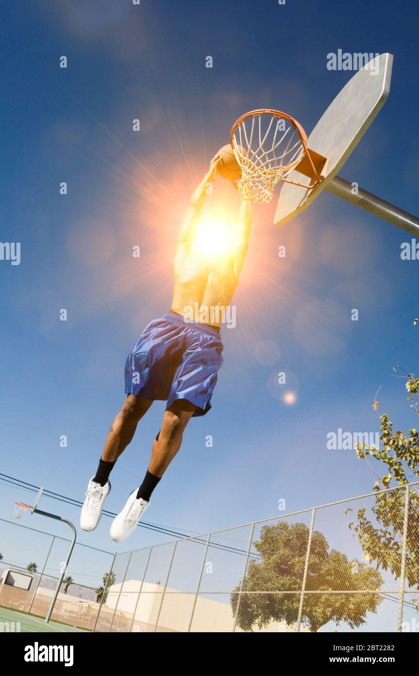 Man about to slam dunk ball on the basketball court with strong sun ...