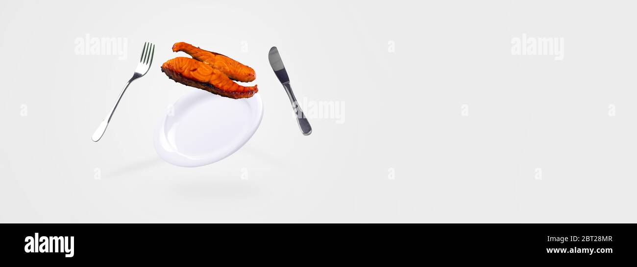 grilled salmon fish falling on the levitating plate, fork and knife ...