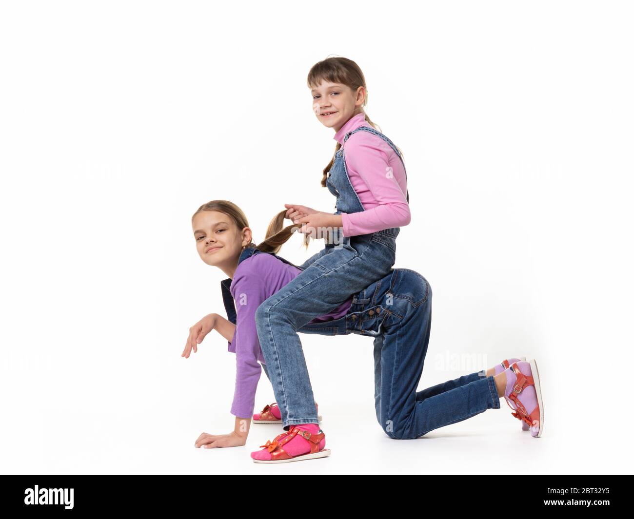 Two girls play horse on a white background Stock Photo - Alamy