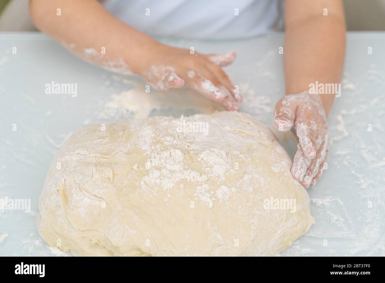 hands of a young child on a yeast dough in flour. the child learns to ...