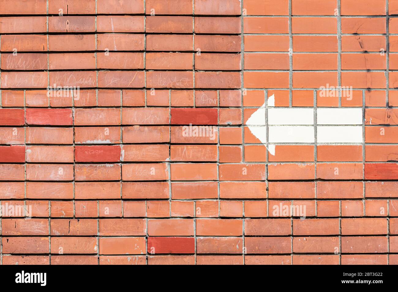 Red brick wall with a painted white arrow pointing in the direction ...