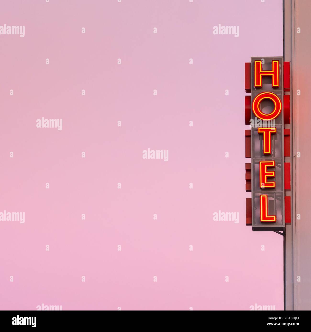 Neon hotel sign on the building corner with pink sunset sky at ...