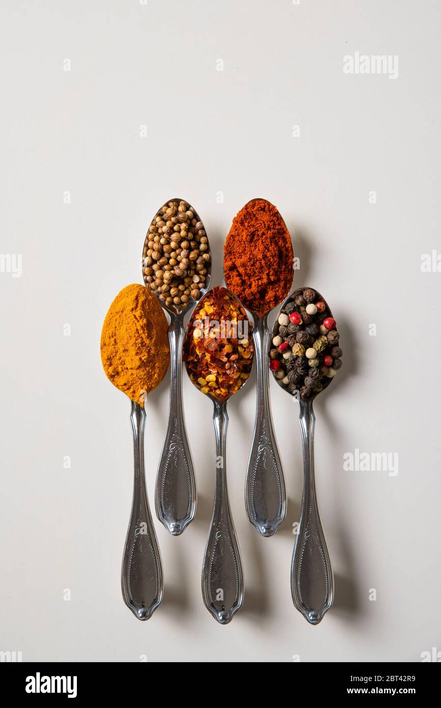 Five small silver spoons with spices isolated on a white background ...