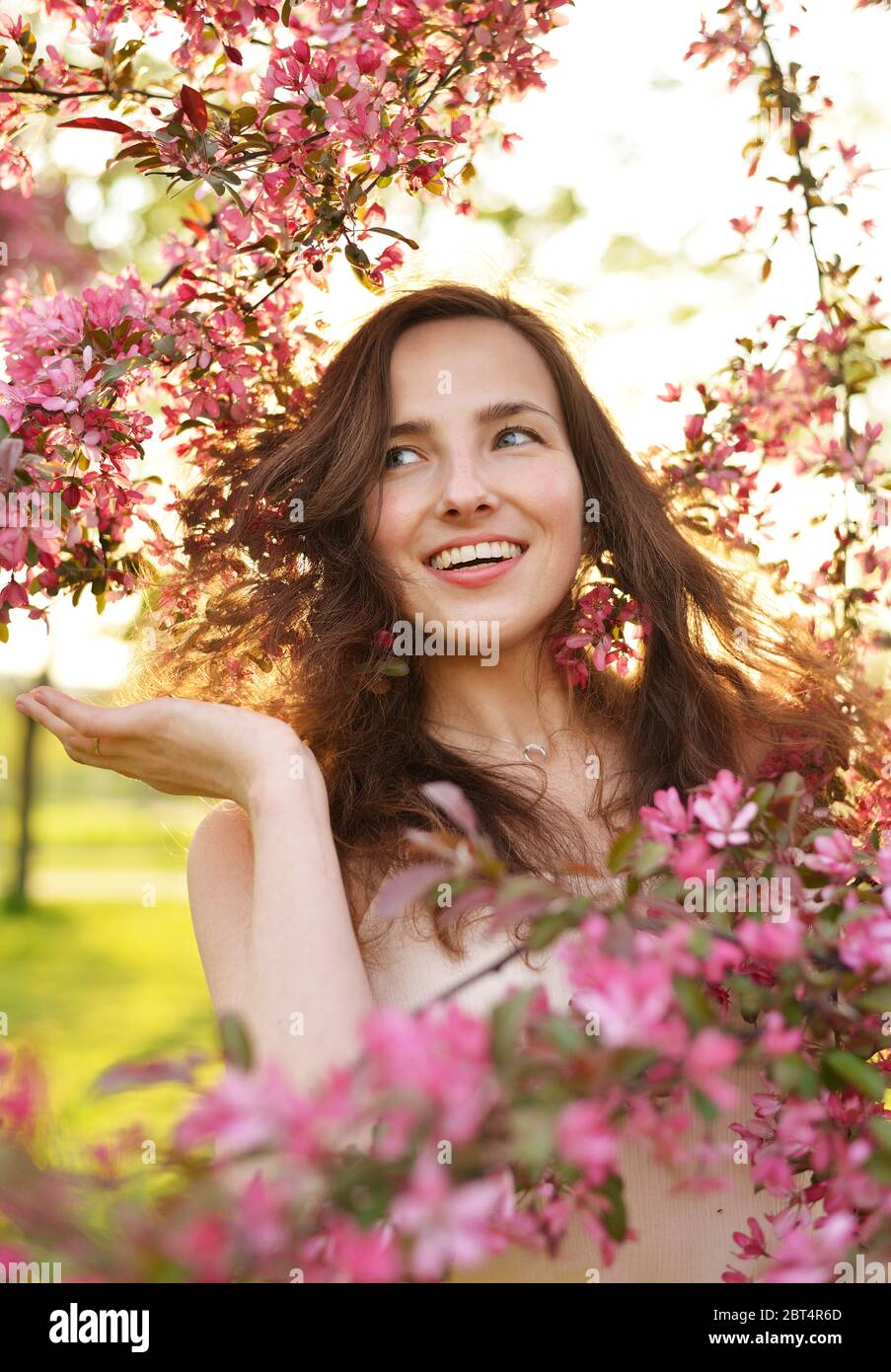 A young beautiful girl is laughing at a fading pink Apple tree in the ...