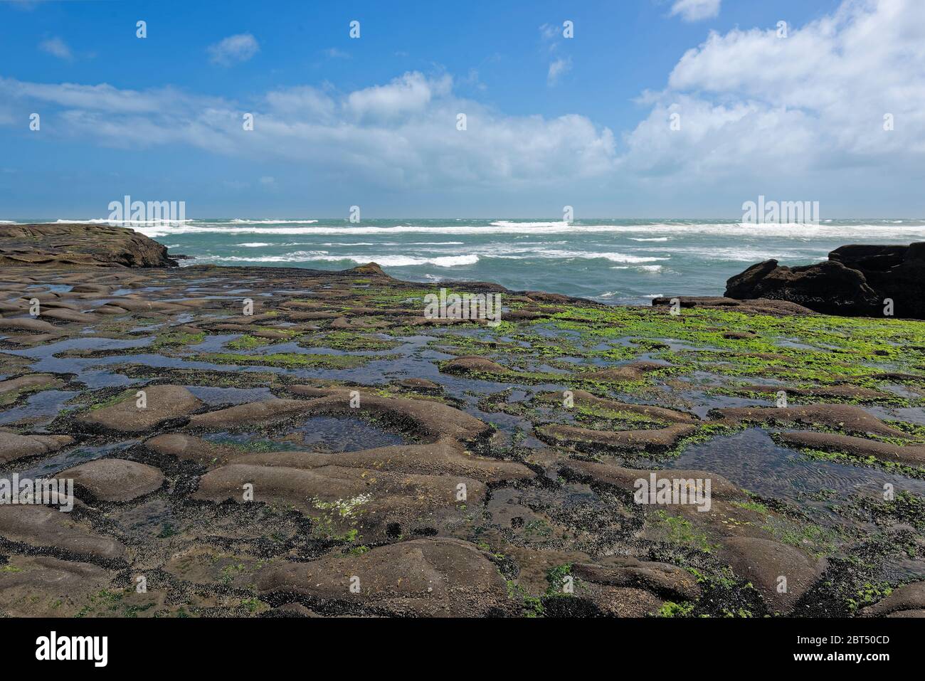 Rough seas under a blue sky with a rocky beach in the foreground ...