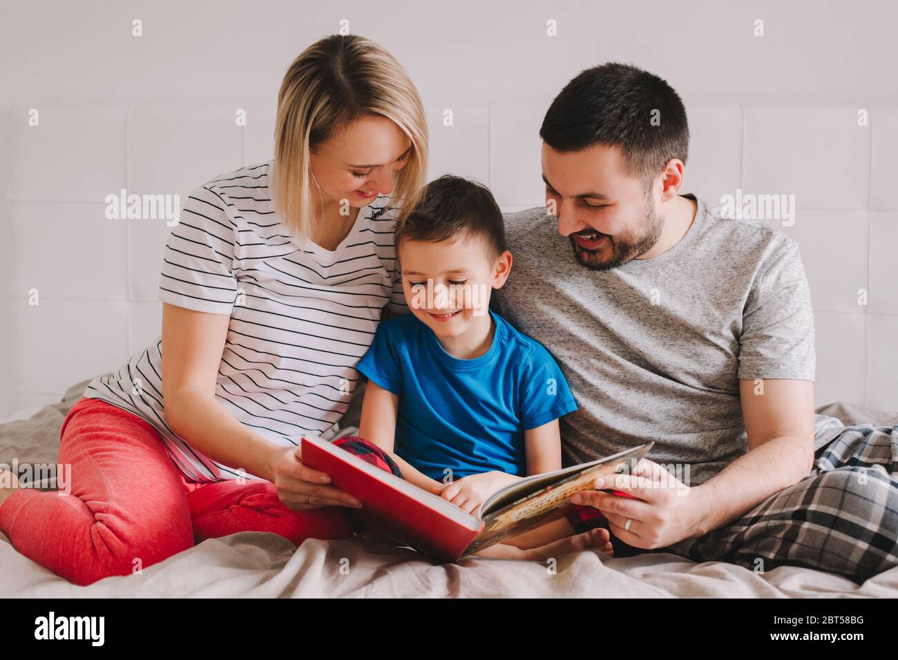 Family of three sitting on bed in bedroom reading book. Mother, father ...