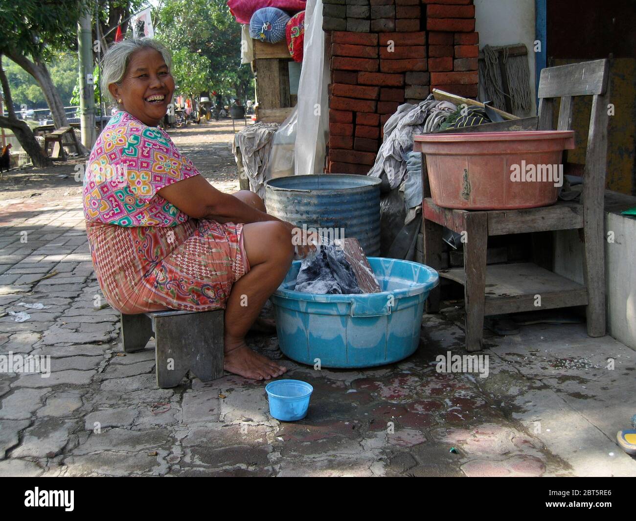 happy smiling woman doing her laundry outdoors using plastic bowl in ...