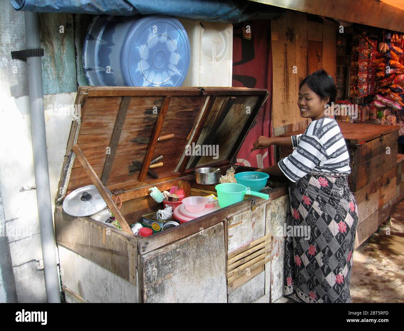 woman preparing meal in large outdoor wooden chest in slum area next to ...