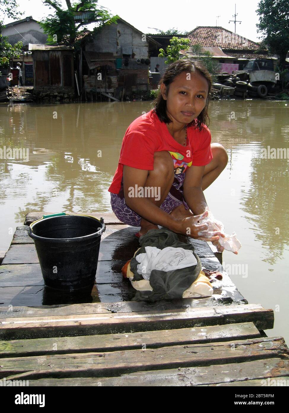 young girl doing laundry using polluted water in slum area next to the ...