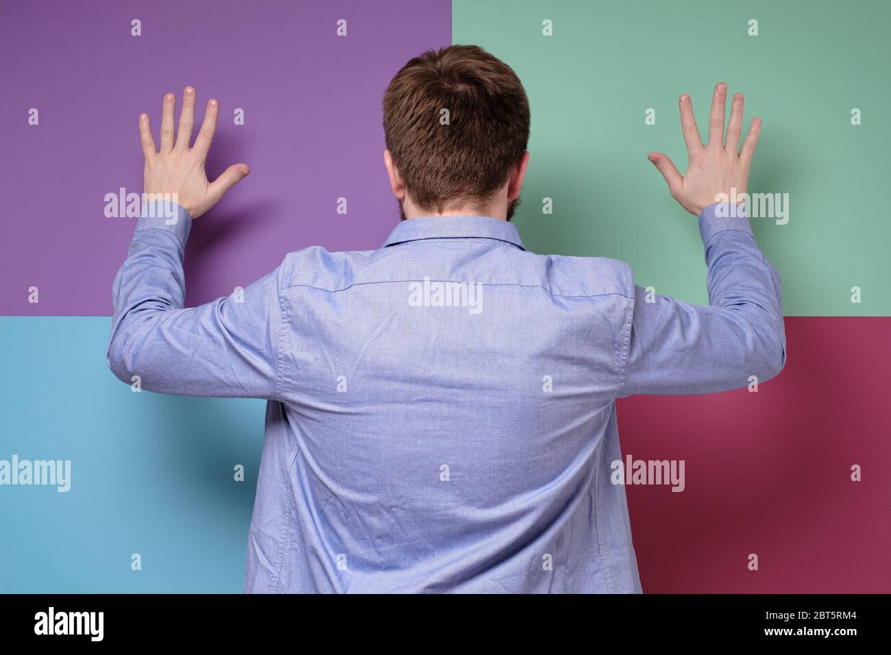 Man in a blue shirt stands with his back to the camera and raises hands ...