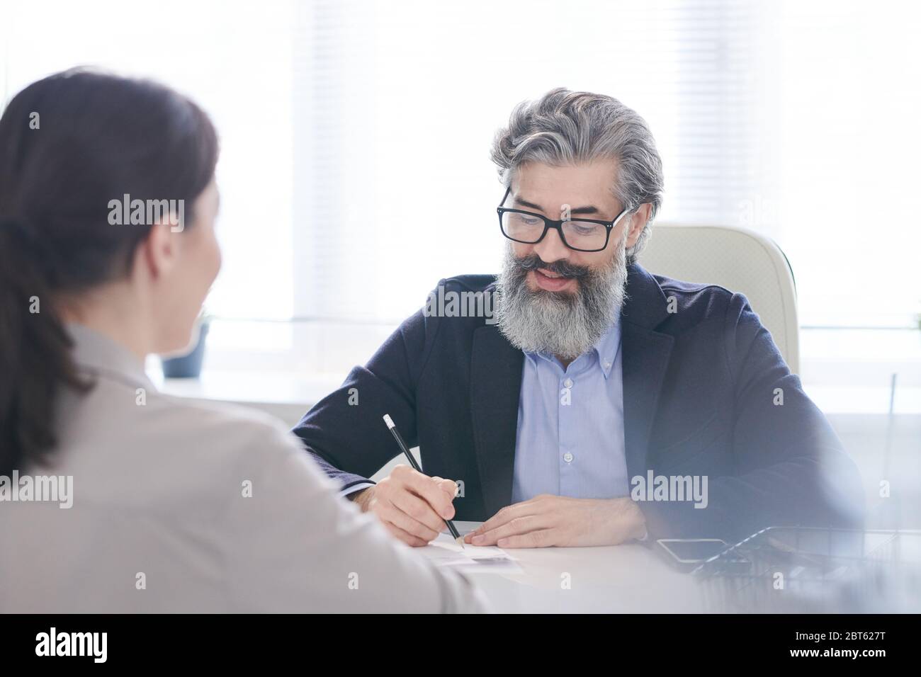 Senior male employer in eyeglasses and formalwear looking through ...