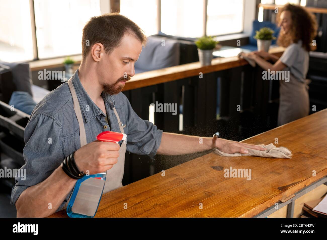 Young serious waiter or worker of cafe or restaurant cleaning bar ...