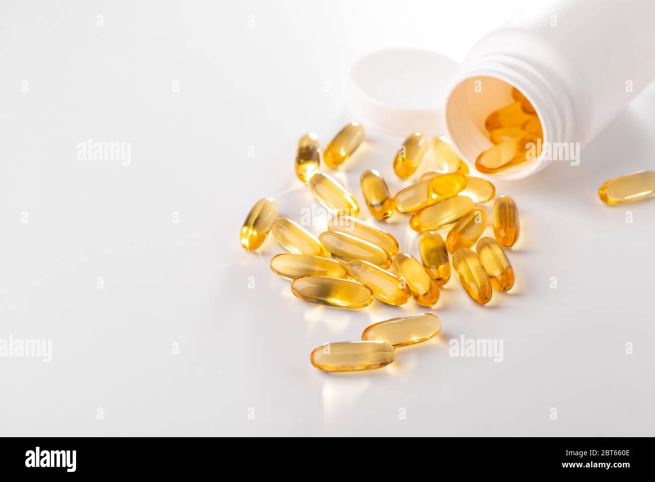 Omega-3 fatty acid capsules scattered from a bottle on white background ...