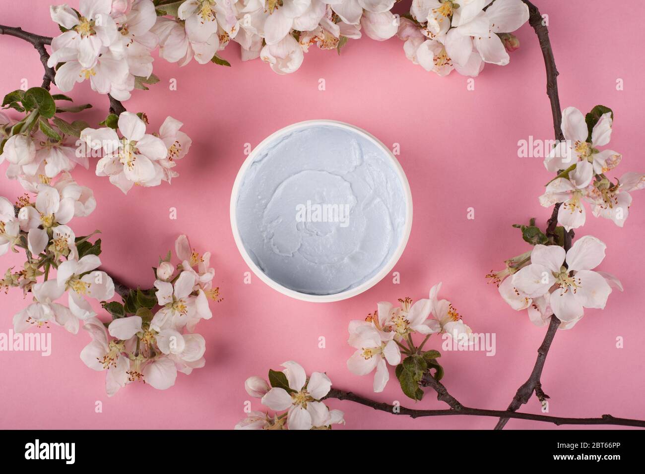 white round body scrub on a pink background with branches of white ...