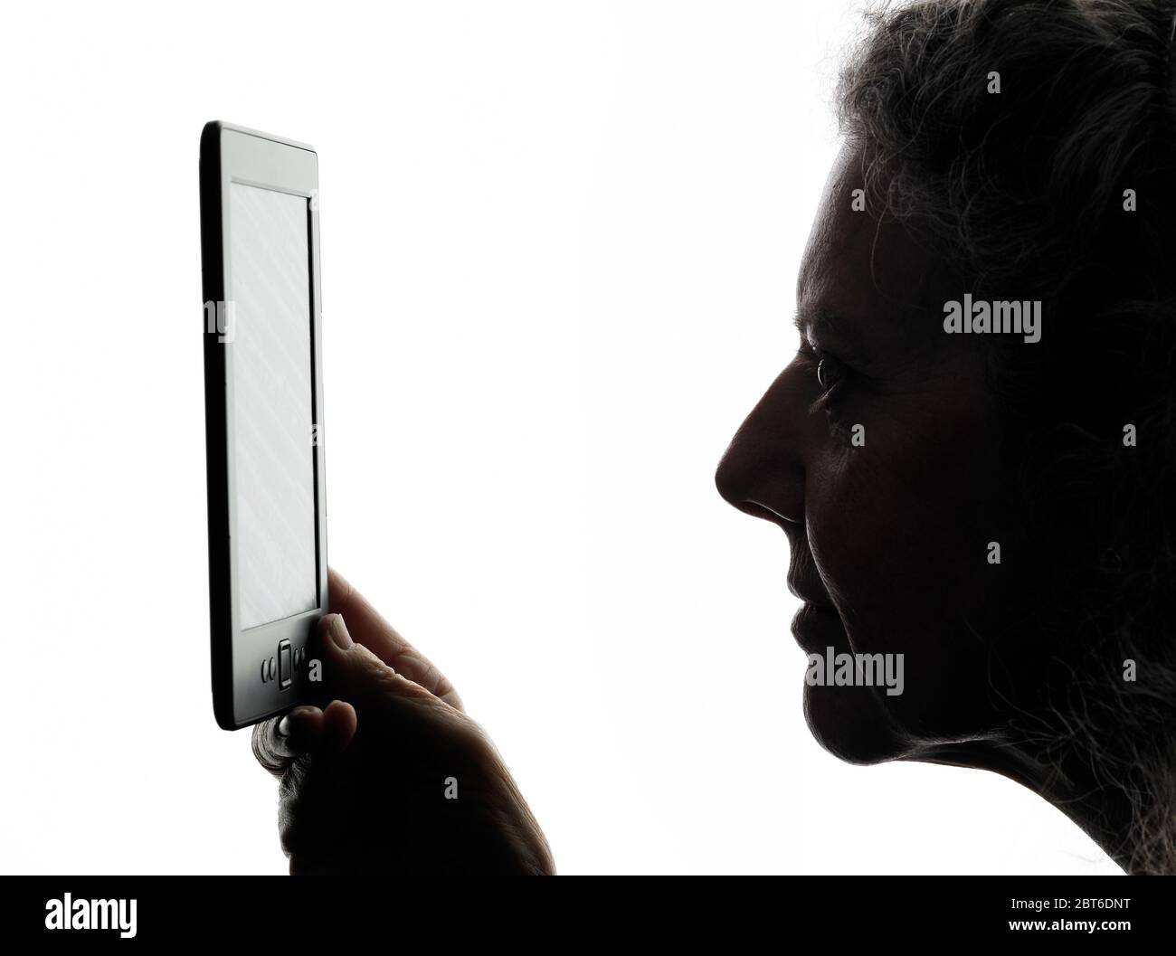 Woman in silhouette reading from hand held small digital tablet screen ...