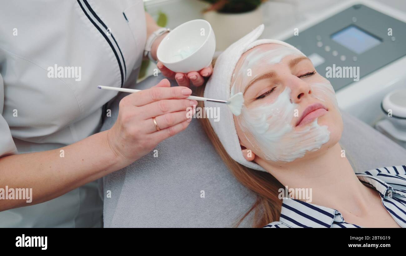 Medium shot of Beautician putting cream mask on woman's face at beauty ...
