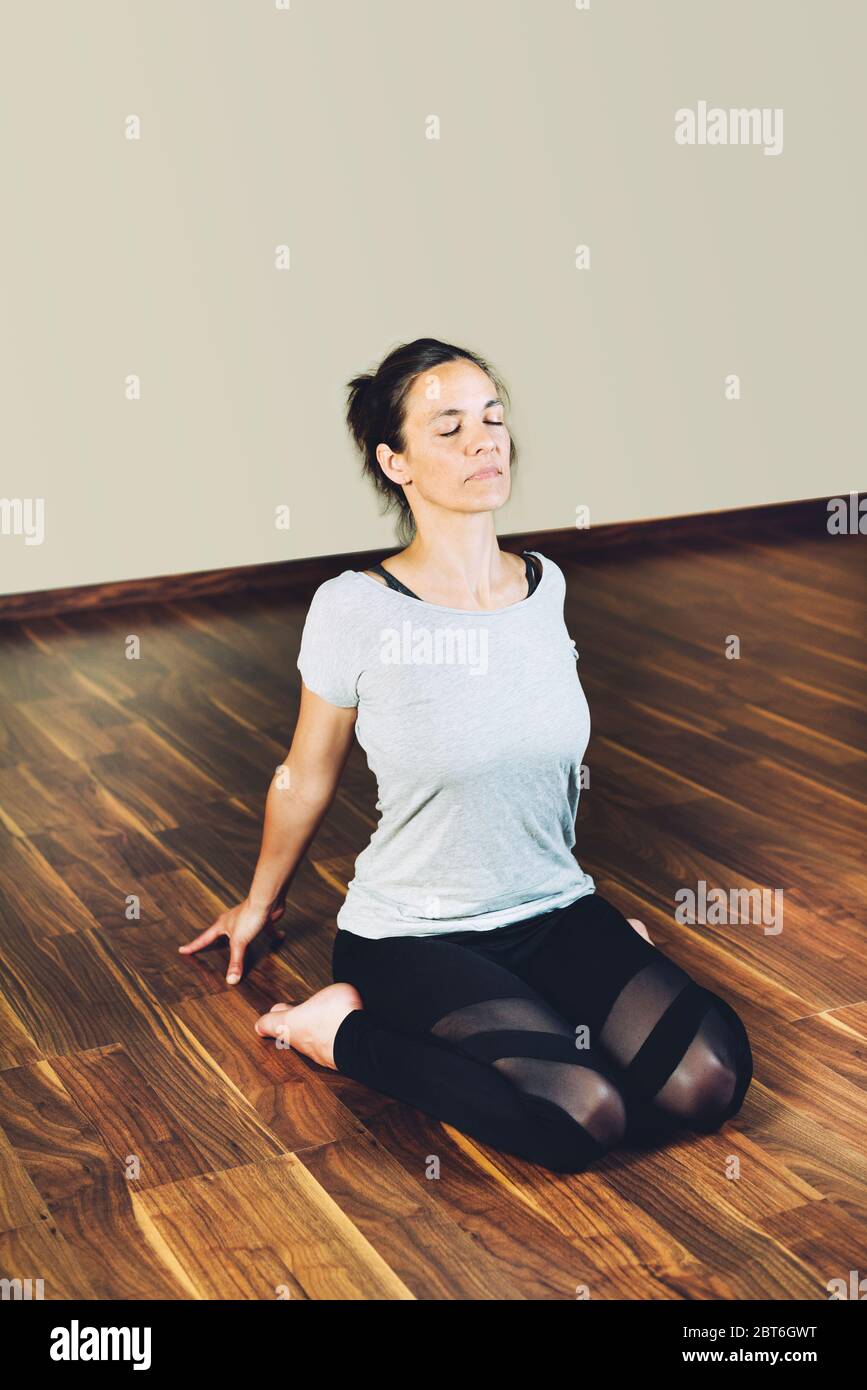 Woman sitting on the floor on her heels and with her arms back ...