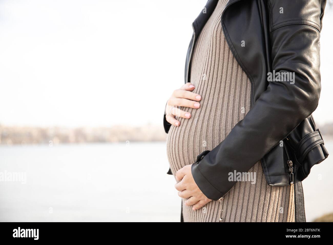 The Pregnant Woman In A Dress Holds Hands On A Stomach Pregnancy