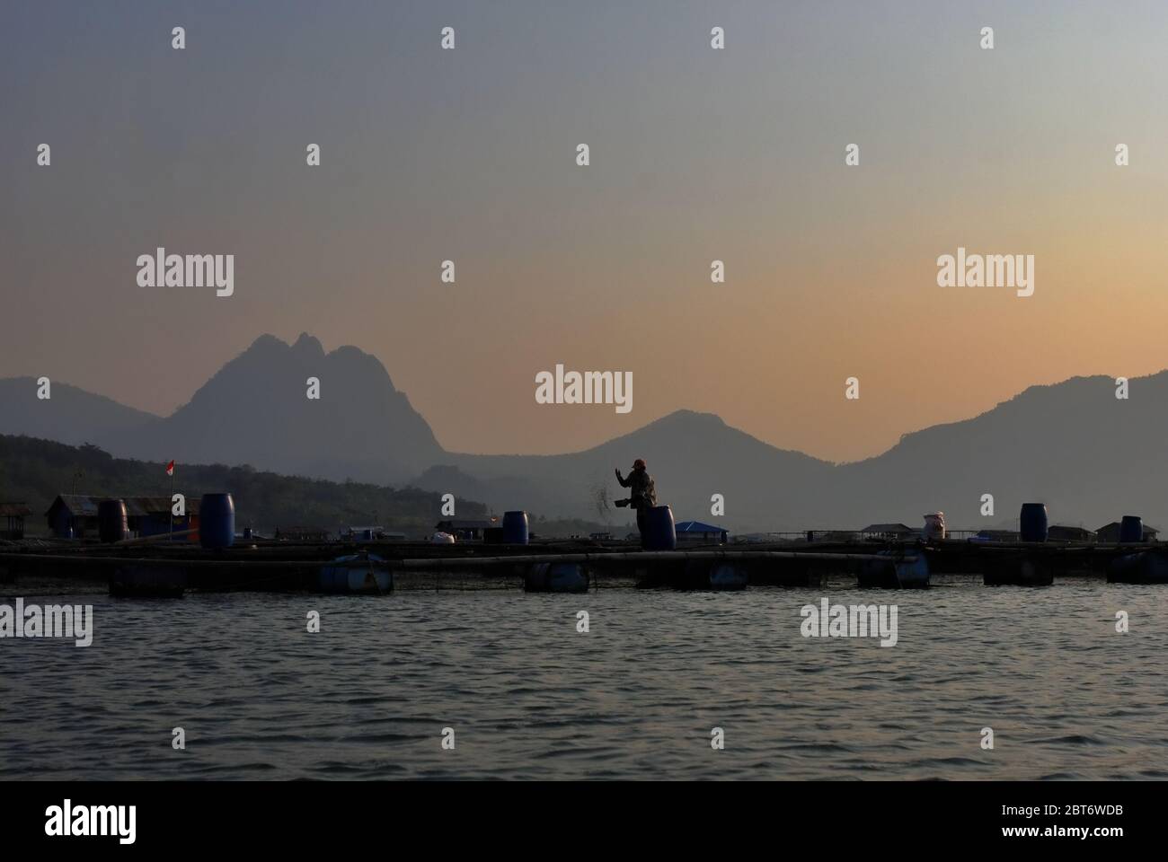 A fish farmer is feeding fish on a floating aquaculture installation on ...