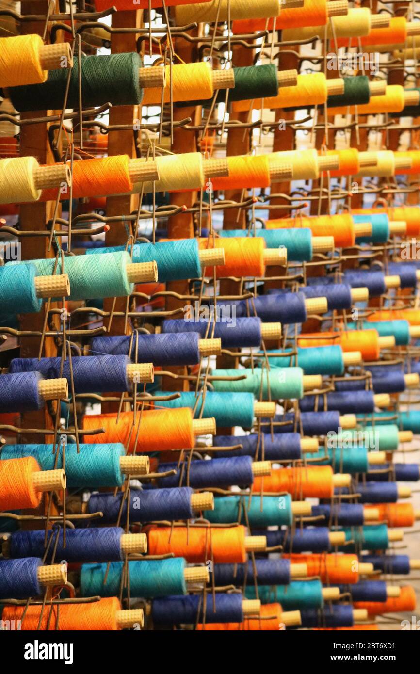 Bobbins of thread in orange, purple, turquoise set in rows in a mill ...