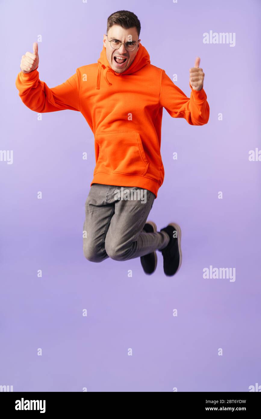 Photo of positive emotional young man jumping isolated over purple ...