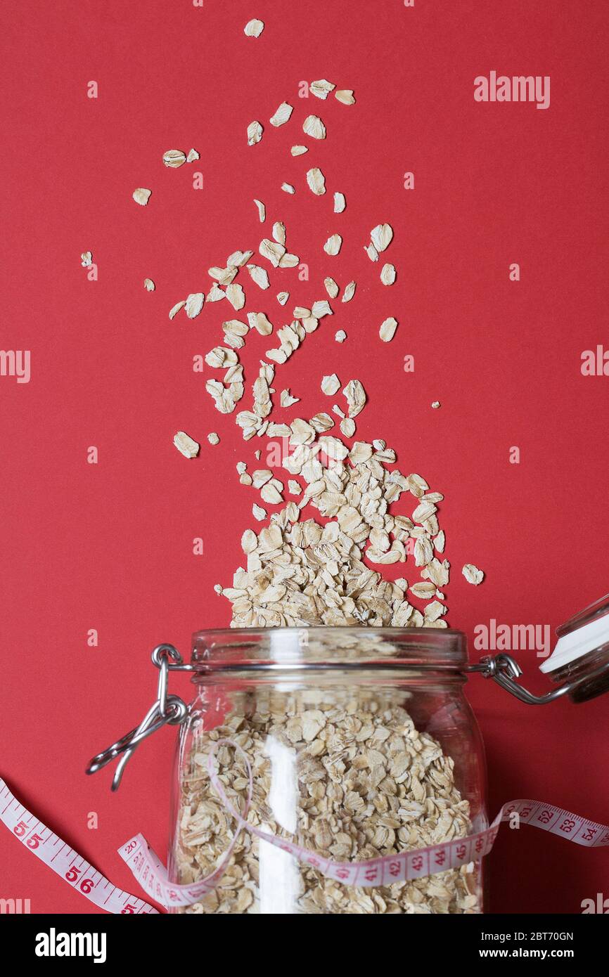Natural oatmeal and measurement on red background . Oatmeal in a glass ...