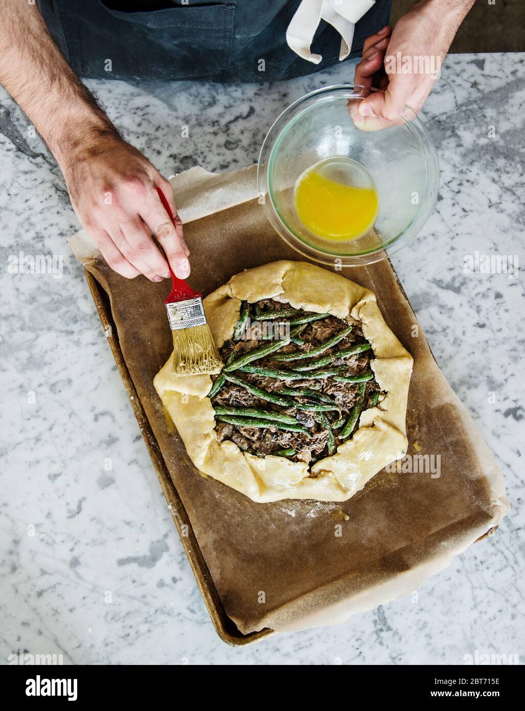 Overhead view of man's hand applying egg wash to galette pie Stock ...