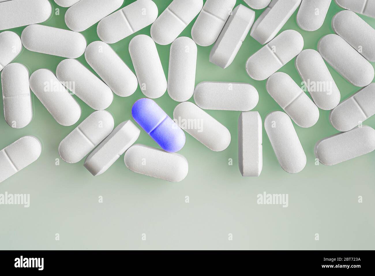 Top view of many white medication capsules or pills and one blue color ...