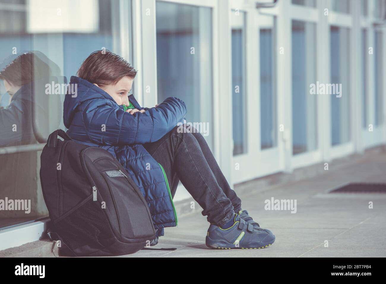 Little boy or child sitting alone on floor in front of the school after ...